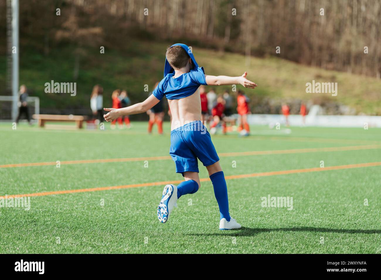 A young athlete in a blue soccer kit joyfully celebrates on a sunny ...
