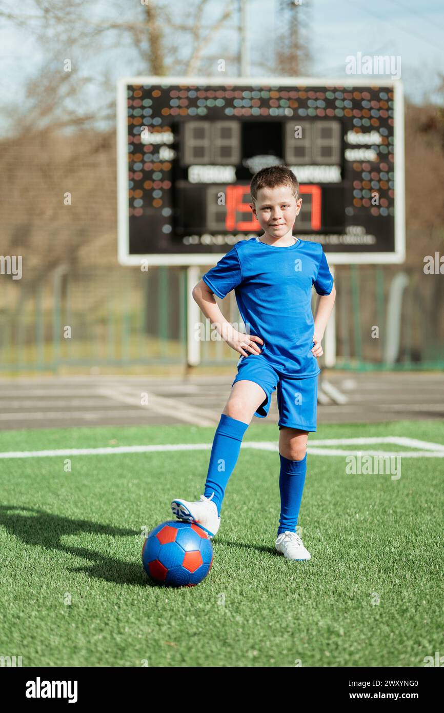 A confident young boy in a blue soccer uniform leans on a red and blue ...