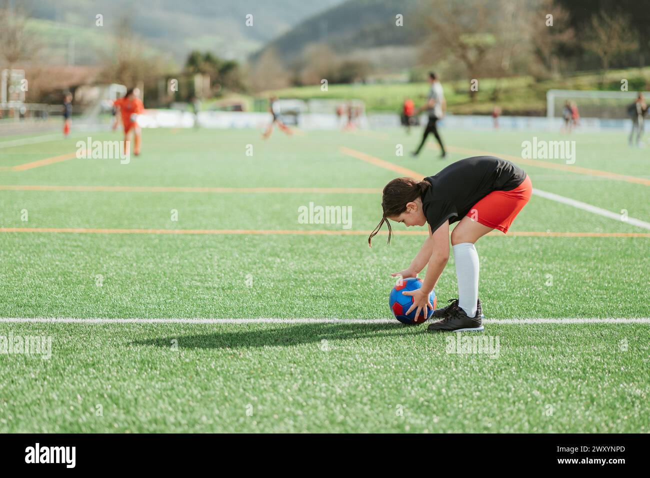 A young female athlete in sportswear is stretching on a soccer field ...