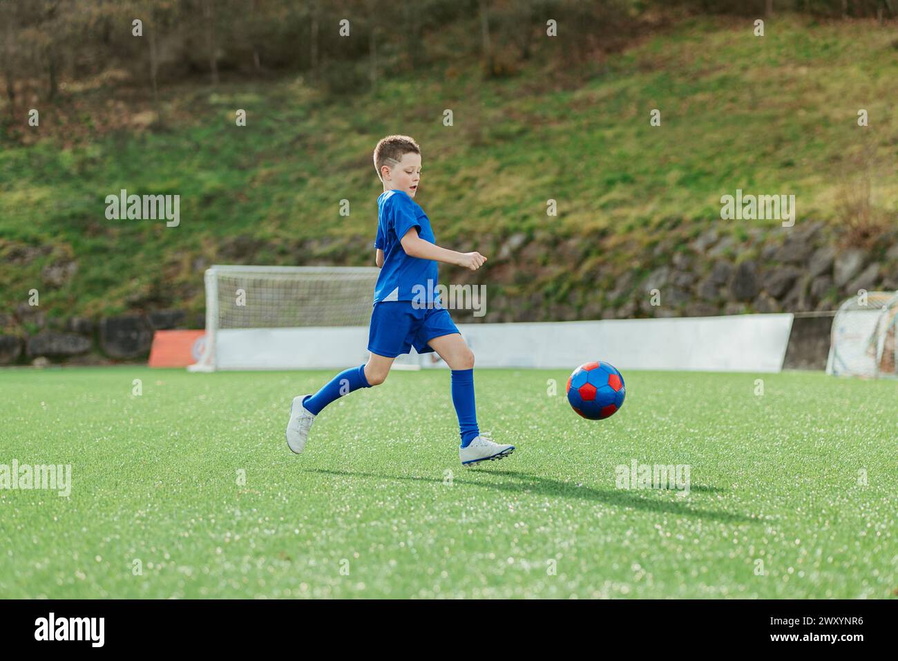 A young boy in blue sports gear kicks a colorful ball while playing ...