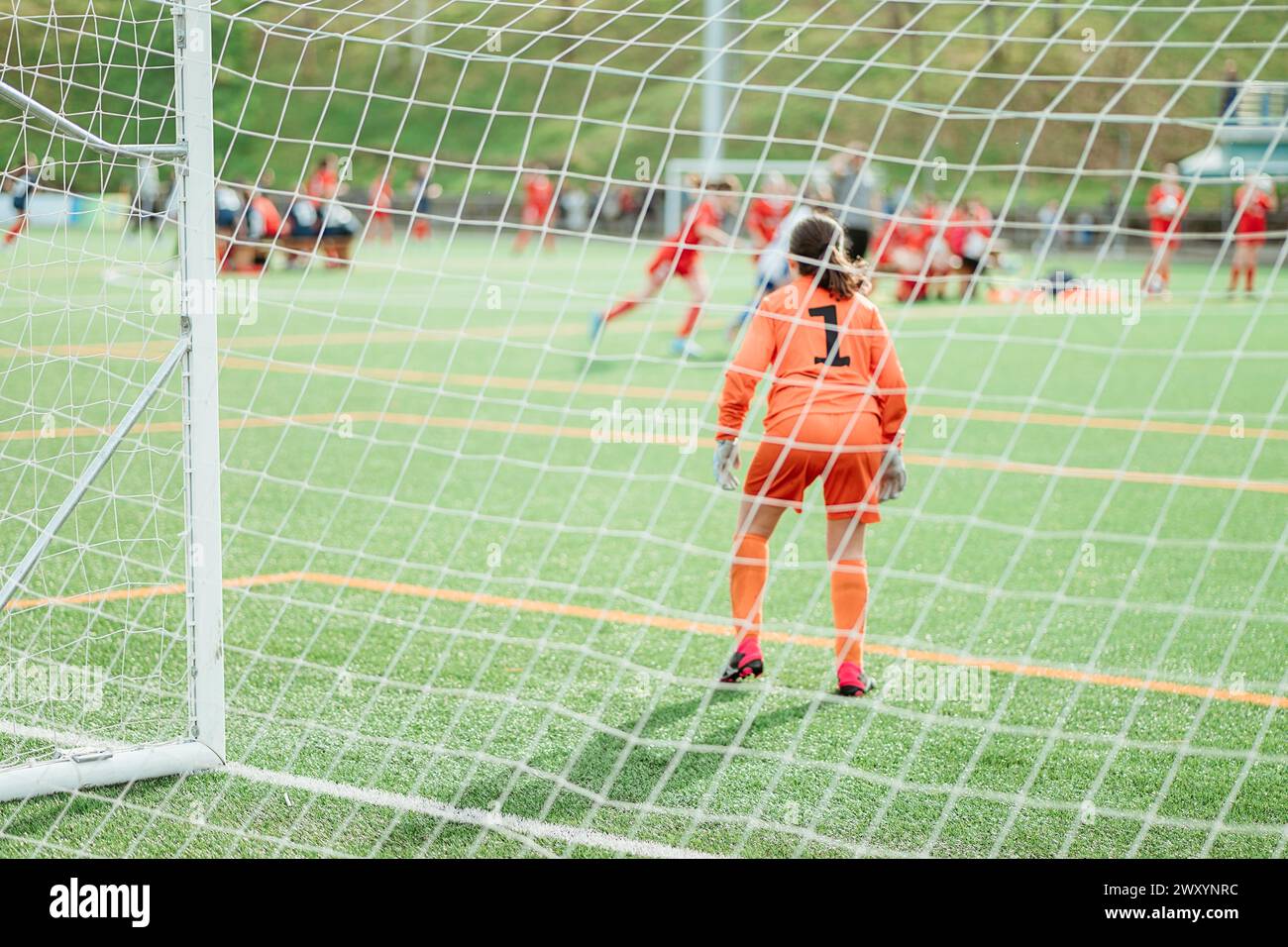 A young soccer player stands in goal, donning an orange uniform and ...