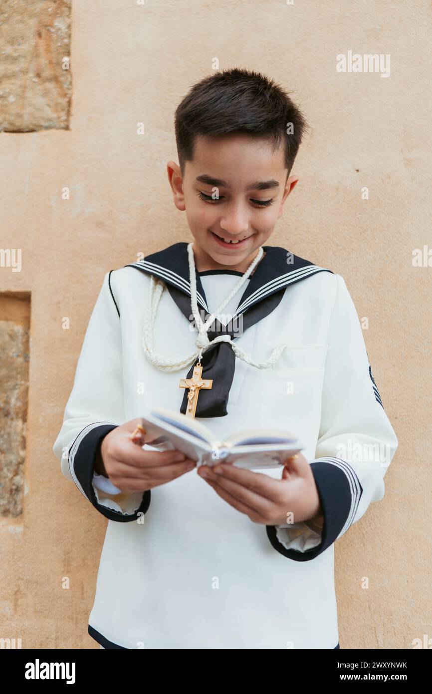 Smiling young boy engaged in reading a prayer book, wearing his First ...