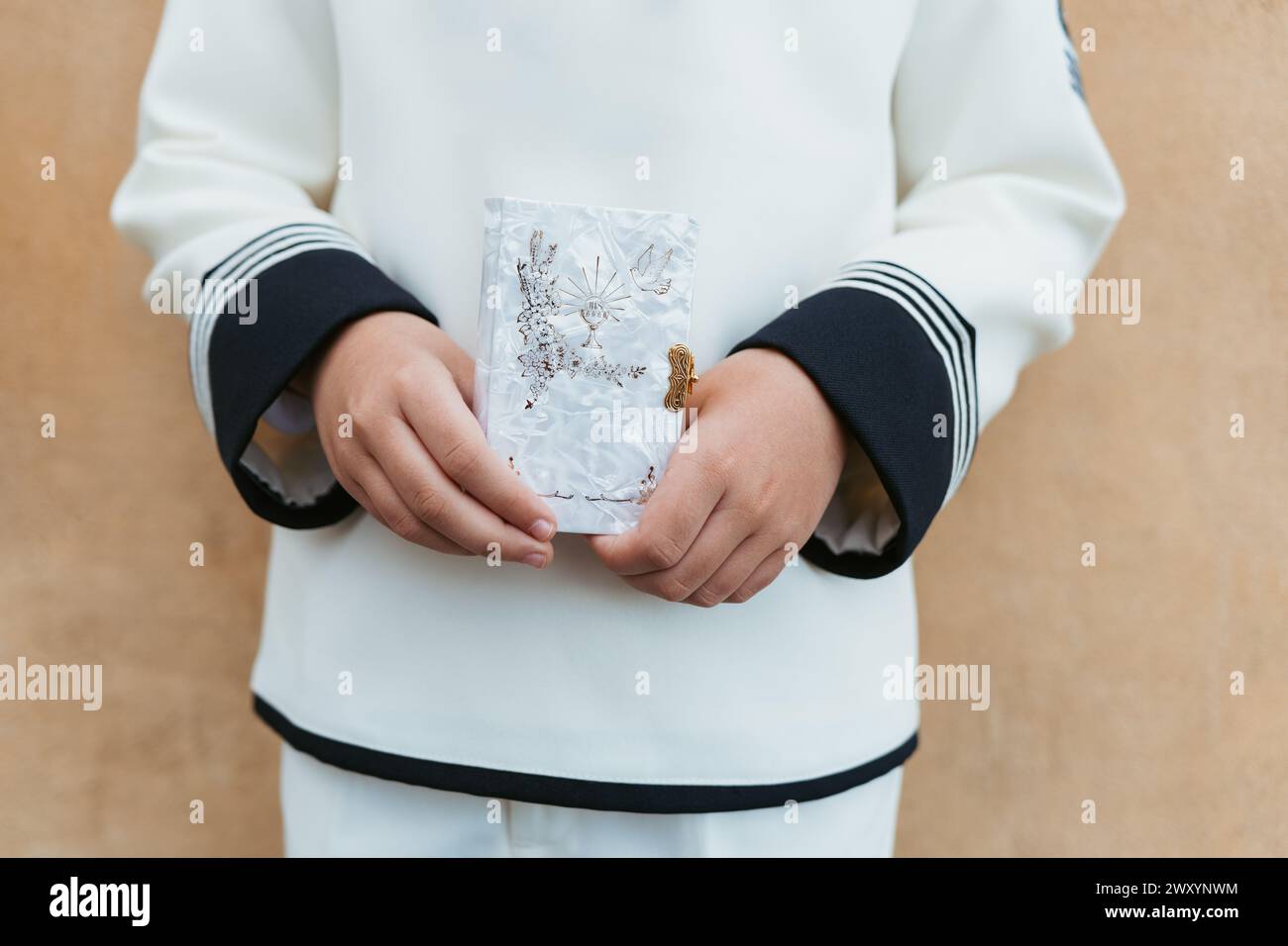 Anonymous child in a white communion suit gently holds a prayer card ...