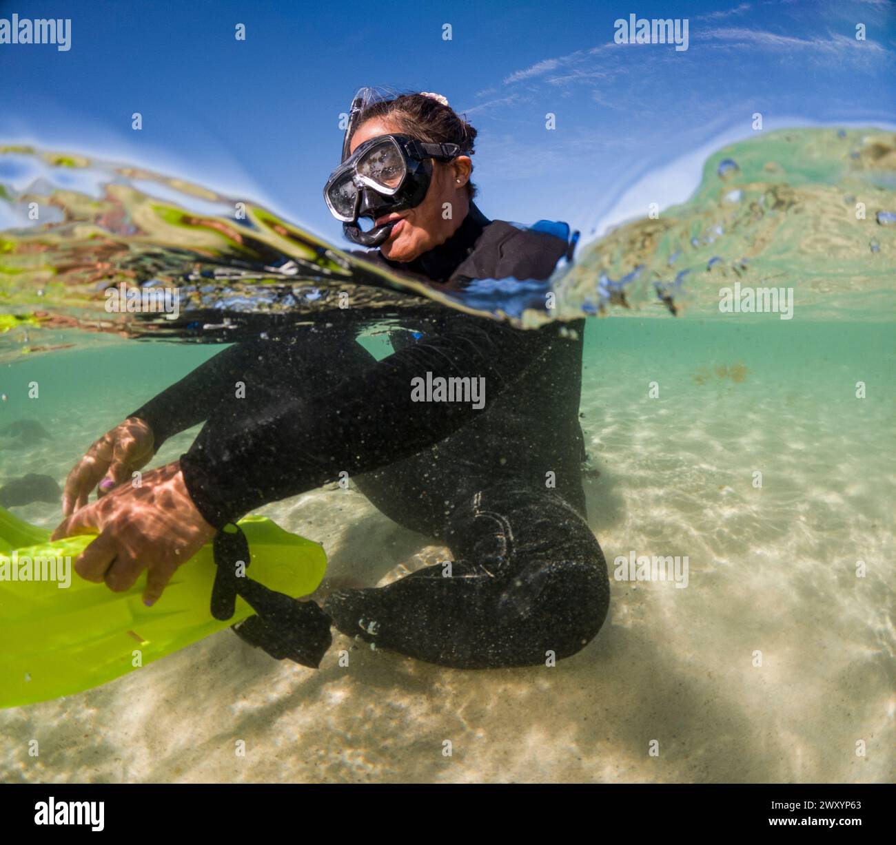 An adventurous snorkeler in a wetsuit is half-submerged in crystal ...