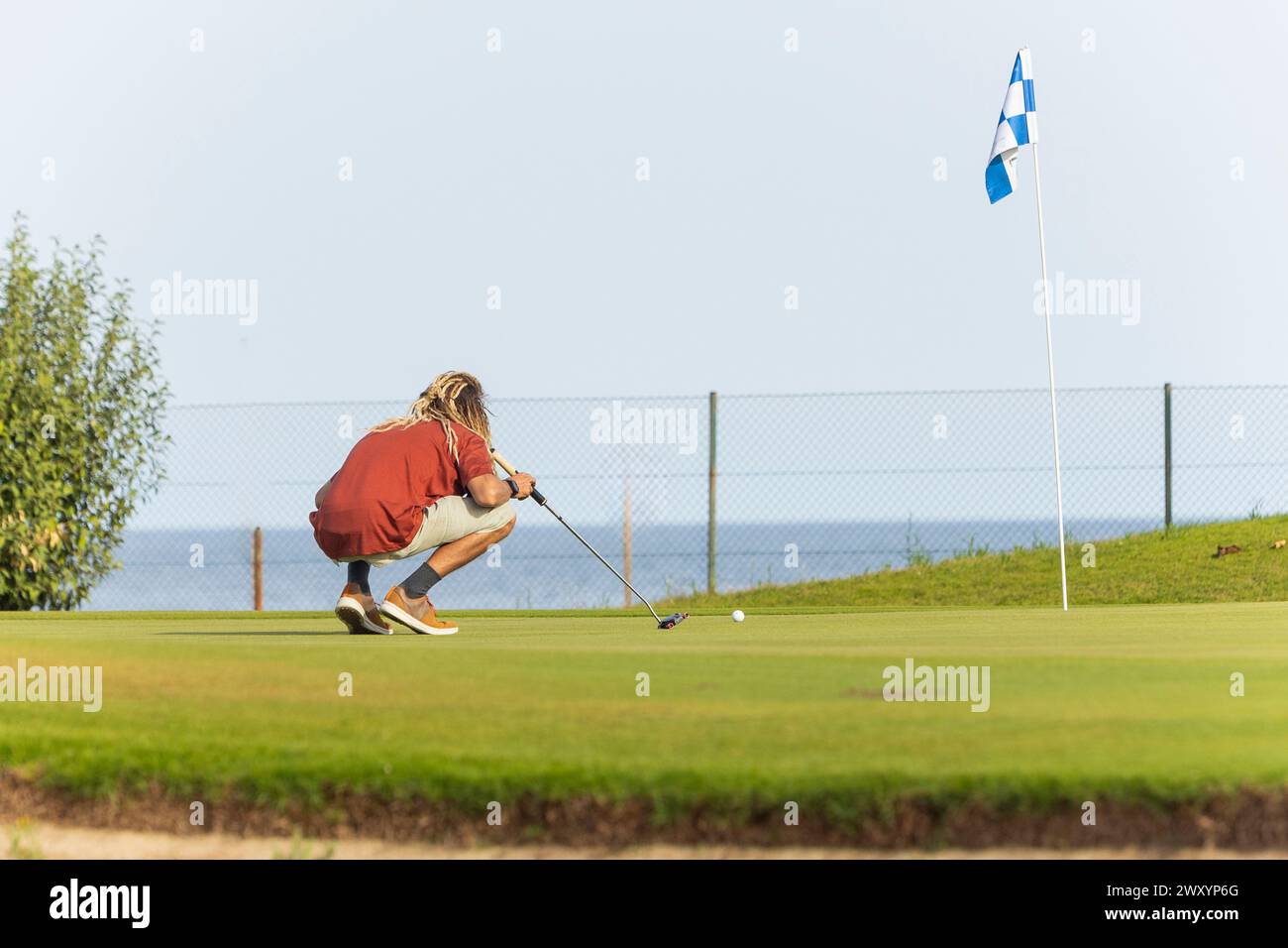 Back view of anonymous Golfer with blonde dreadlocks crouches to align ...