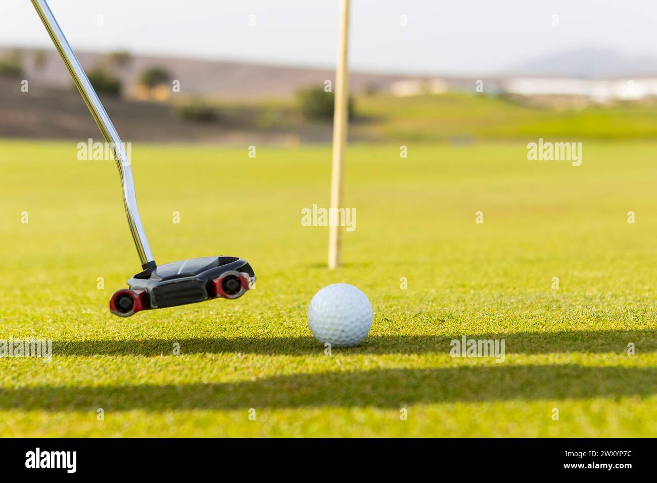 A close-up image of a golf ball on a lush green field, with the putter ...