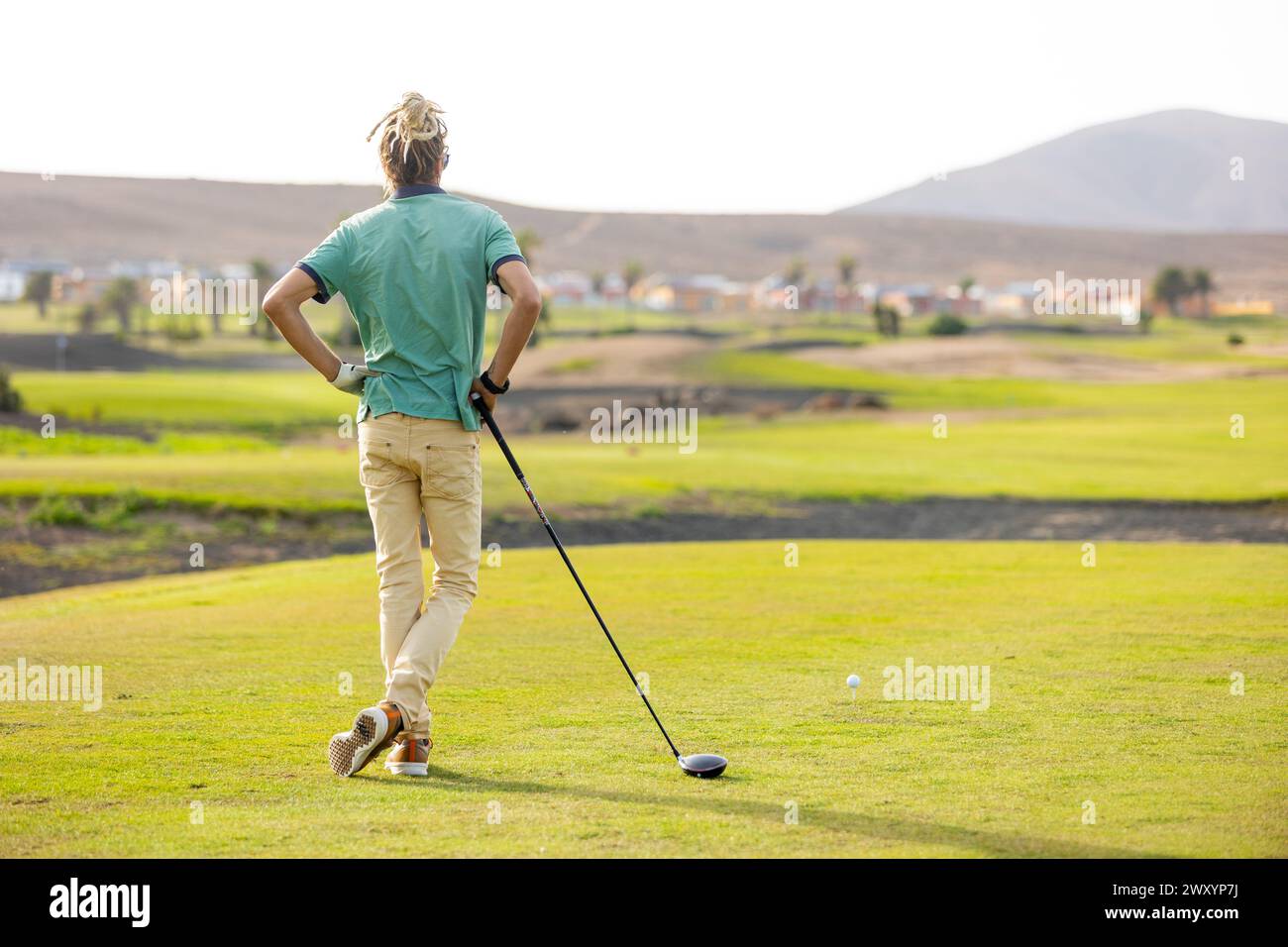 Back view of a golfer stands ready to tee off on a lush green fairway ...
