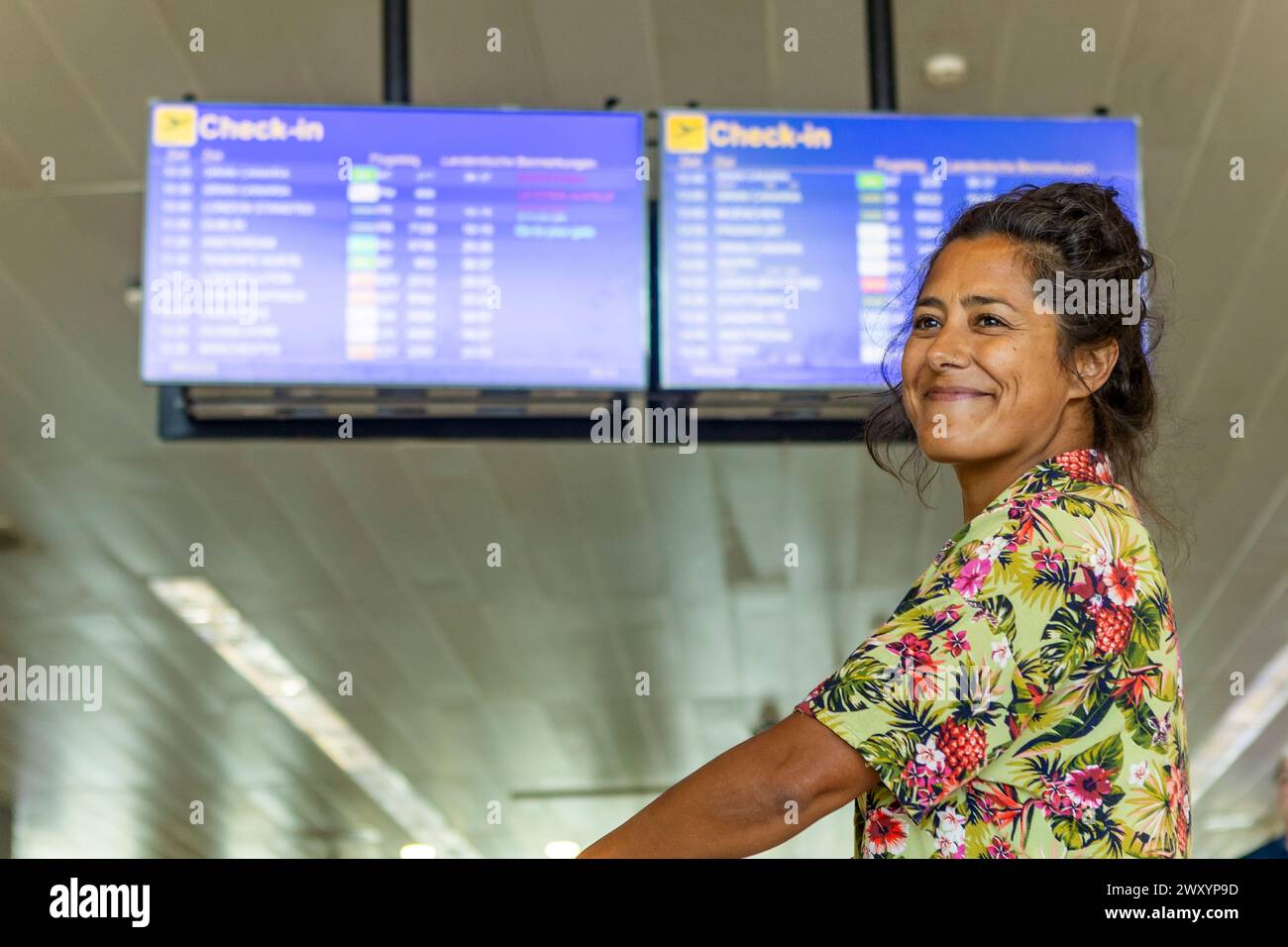 A cheerful woman stands at an airport check-in area, with flight ...
