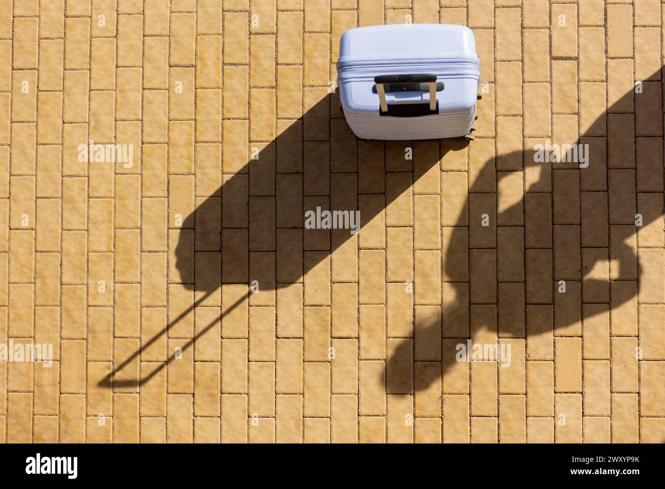 Overhead view of a suitcase casting a long shadow on a yellow brick ...