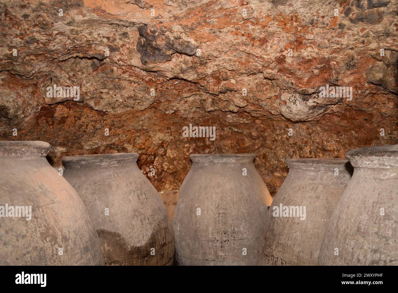 Row of large, old clay jars for wine storage line the stone walls of an ...