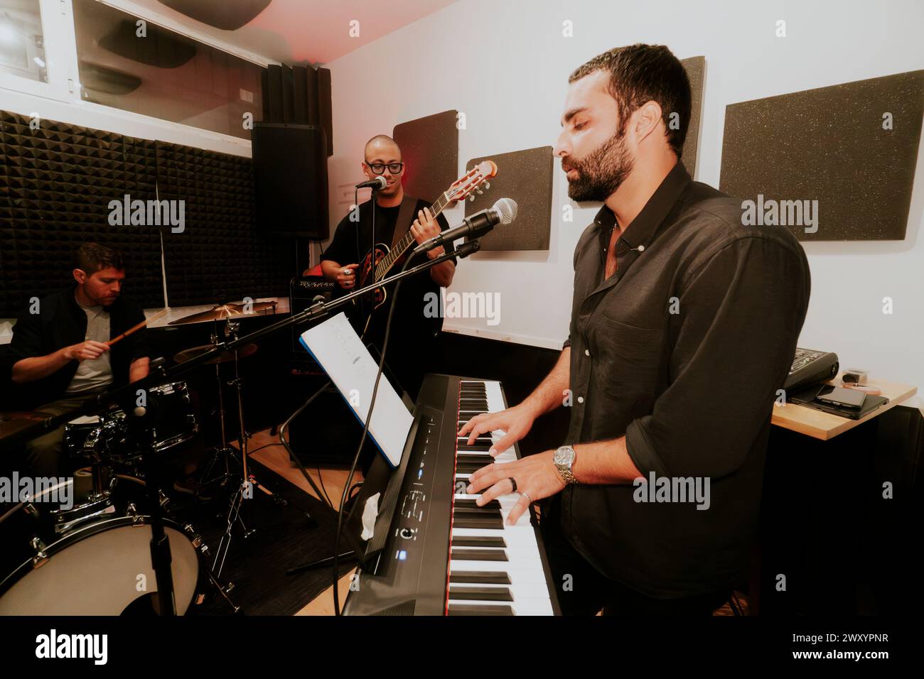 A male trio band intensely performs in a soundproof studio, with ...