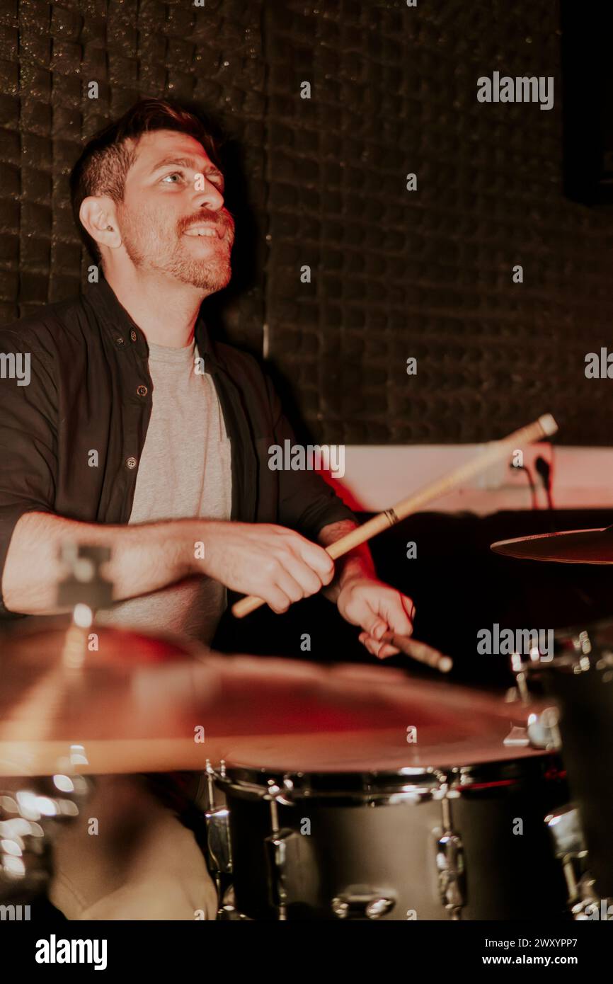 A male drummer is captured mid-performance, looking away from the ...