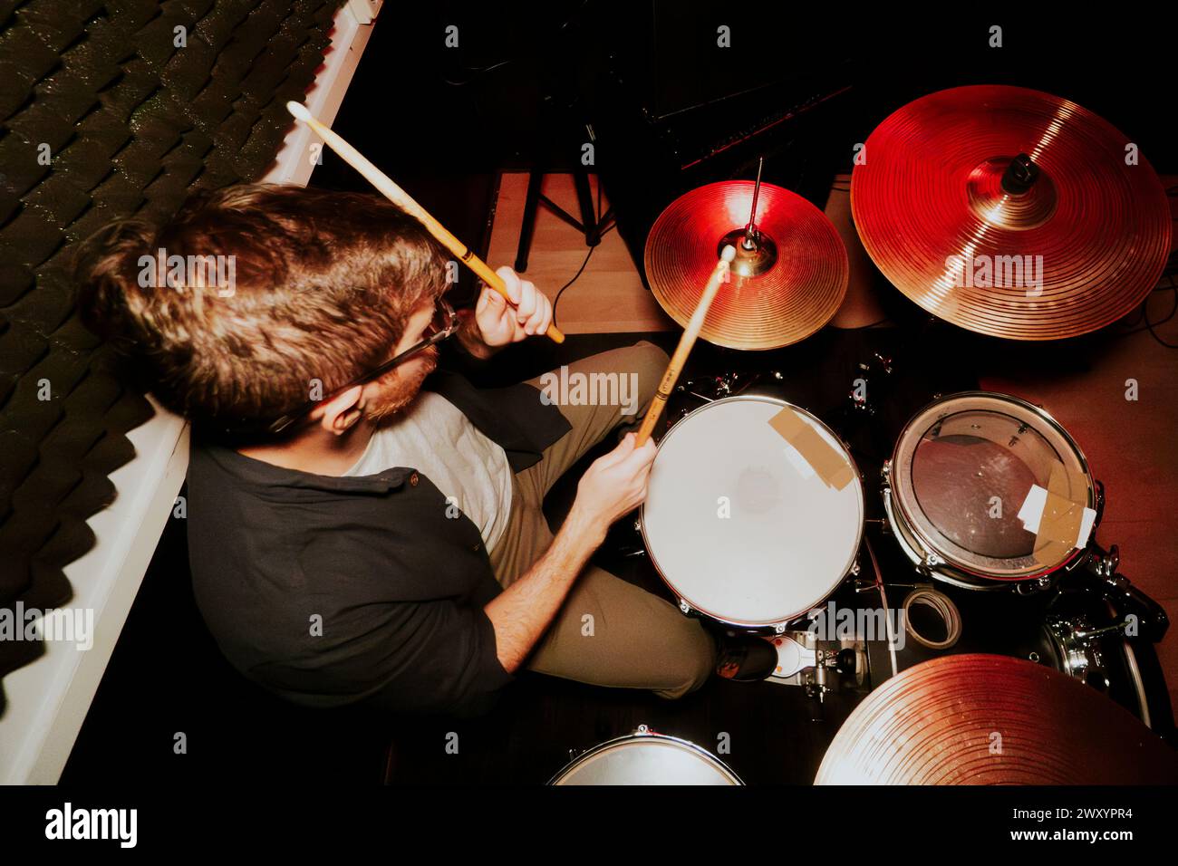 From above male drummer looking away focuses intently on his drum set ...