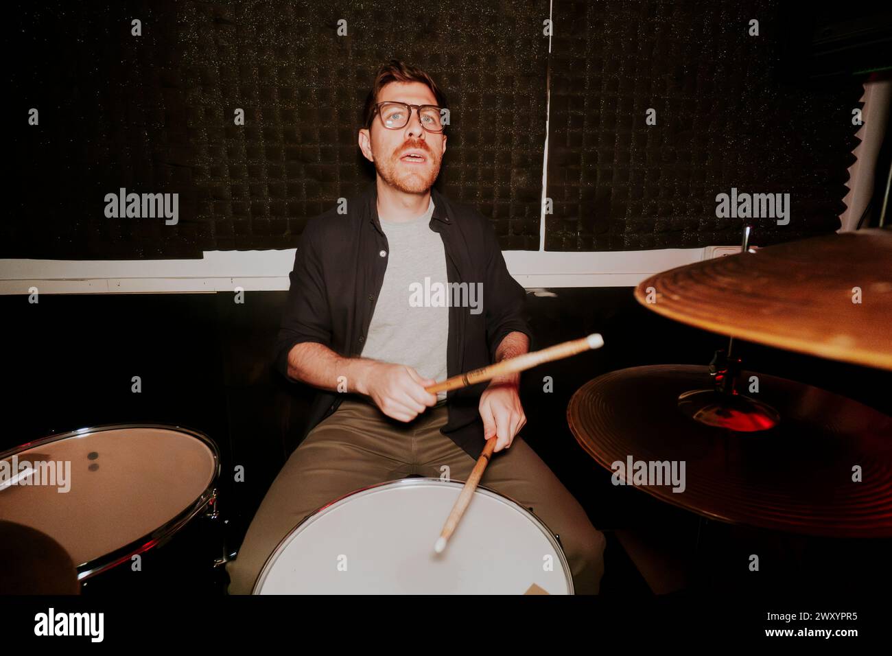 Male drummer looking at camera, absorbed in playing a drum set in a ...