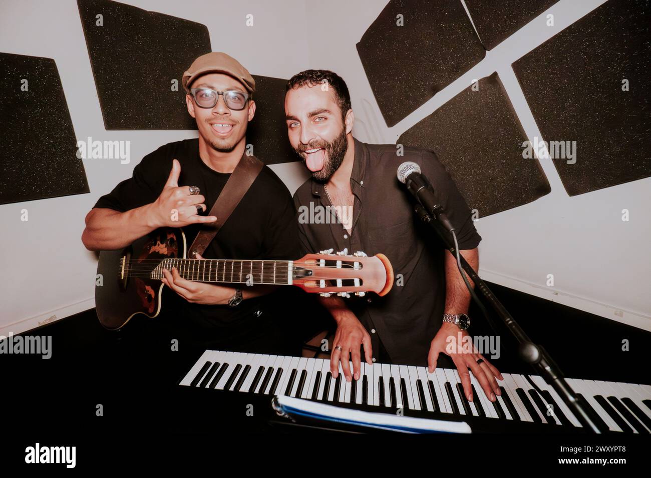 Two men in a band setup play guitar and keyboard while looking at the ...
