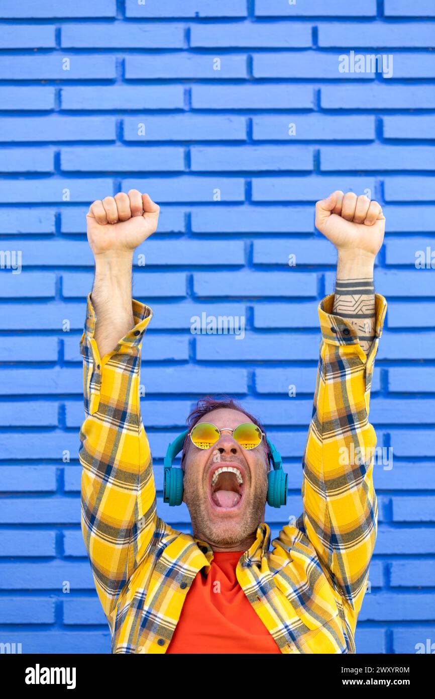 An elated man with headphones and sunglasses shouts in triumph, fists ...