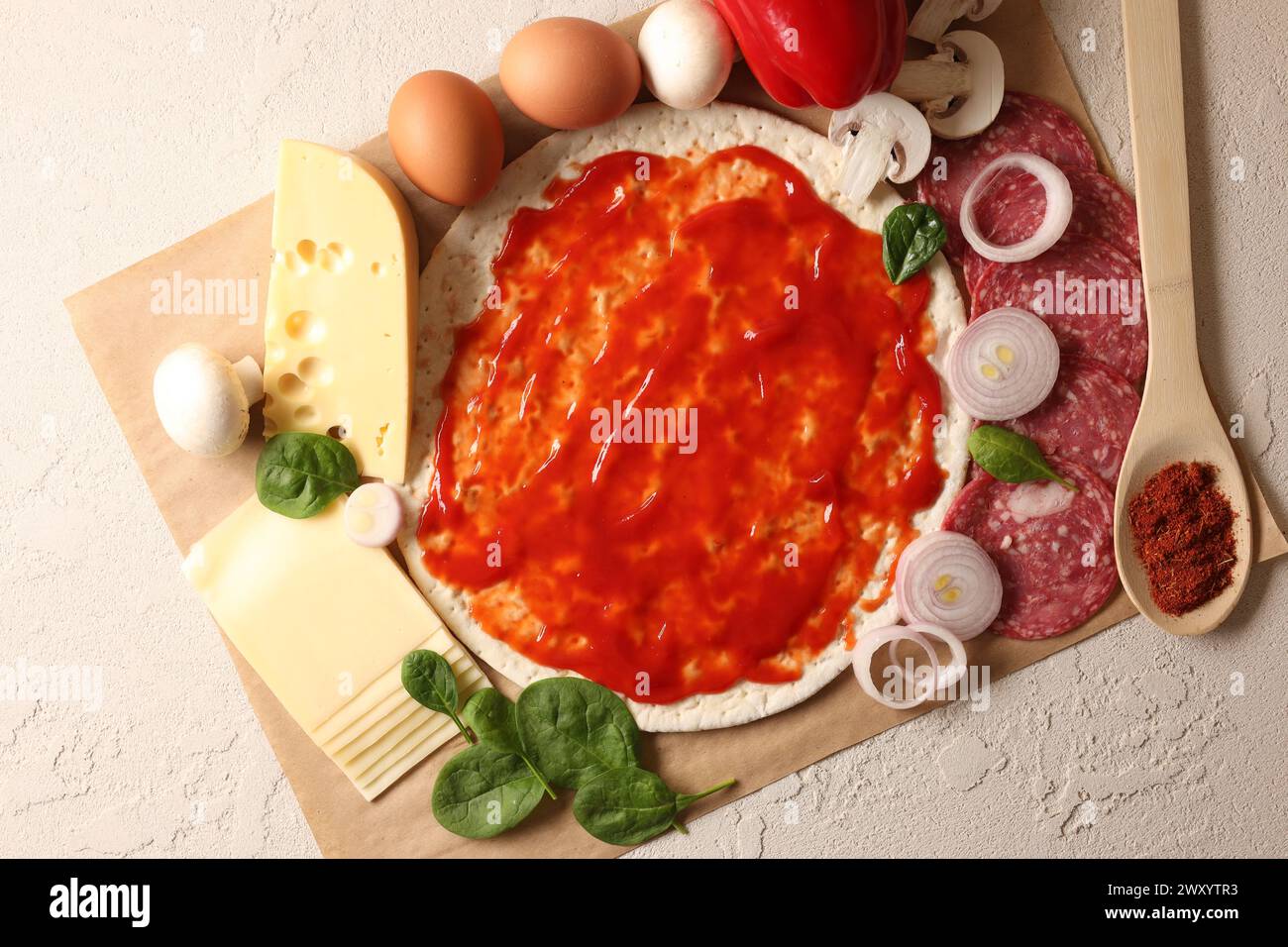 Pizza base smeared with tomato sauce and products on light textured ...