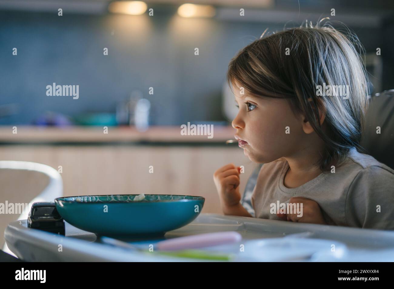 Little kid girl eating her morning porridge rice herself, sitting in ...