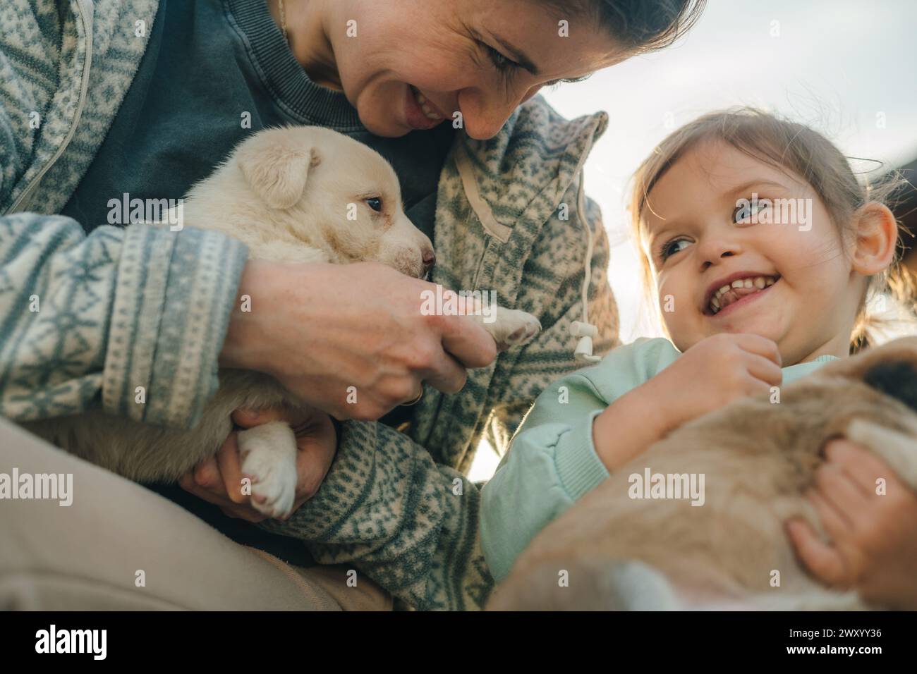 Cute, little girl and her mom holding two puppy dogs pet. Kids and pets ...