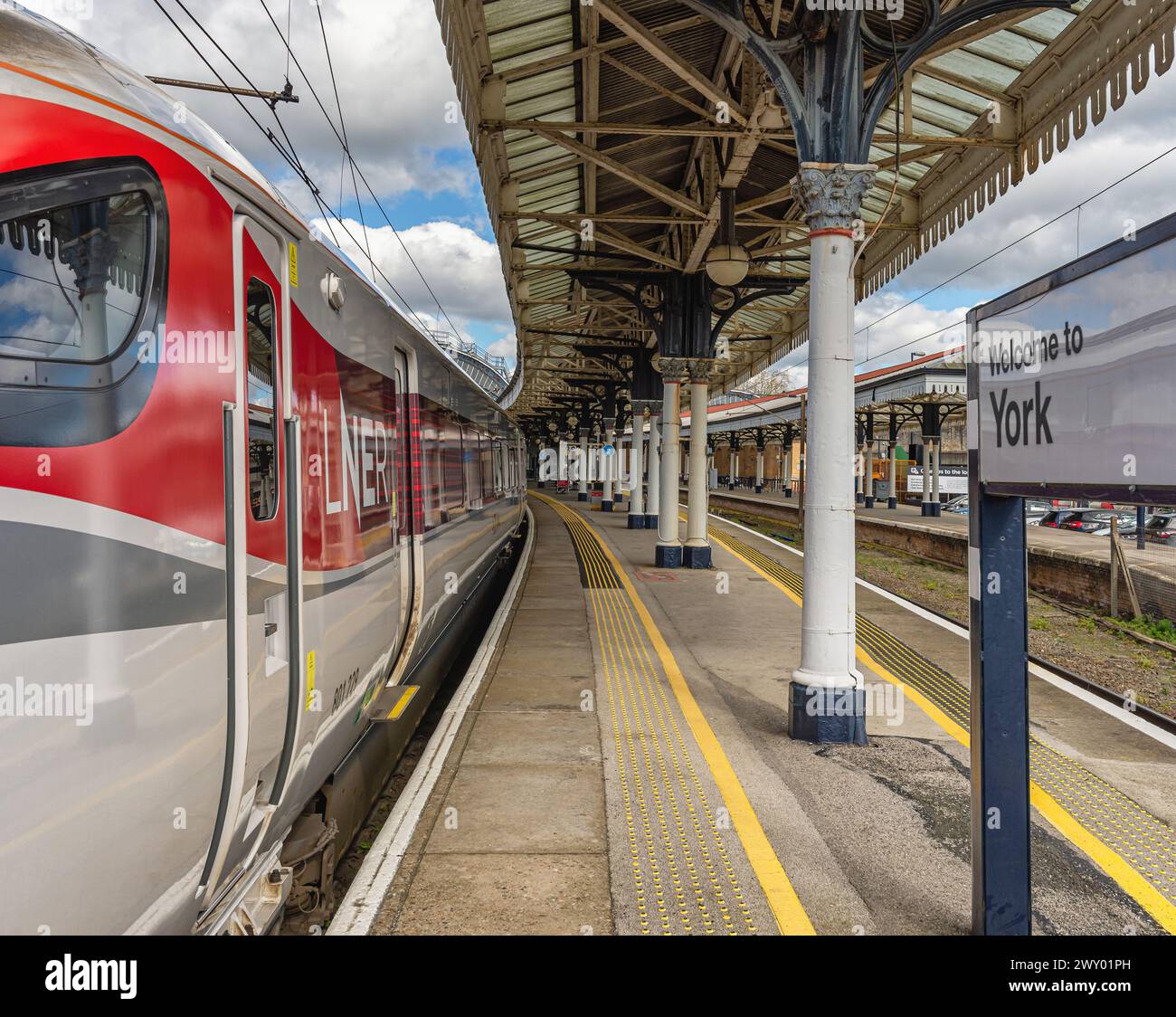 A train waits at a railway station platform beside a historic 19th ...