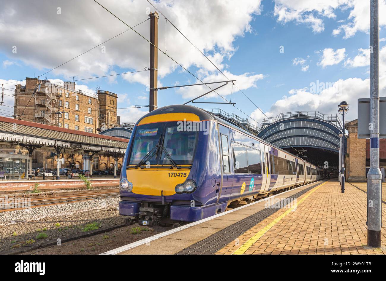 A train emerges from underneath a historic metal arch. A brick hotel ...