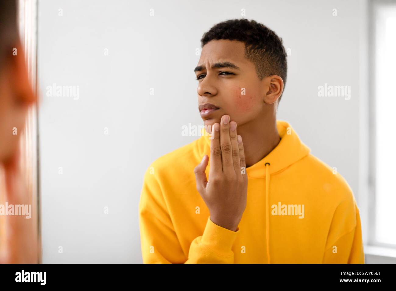 Concerned black teen guy examining face in the mirror Stock Photo - Alamy