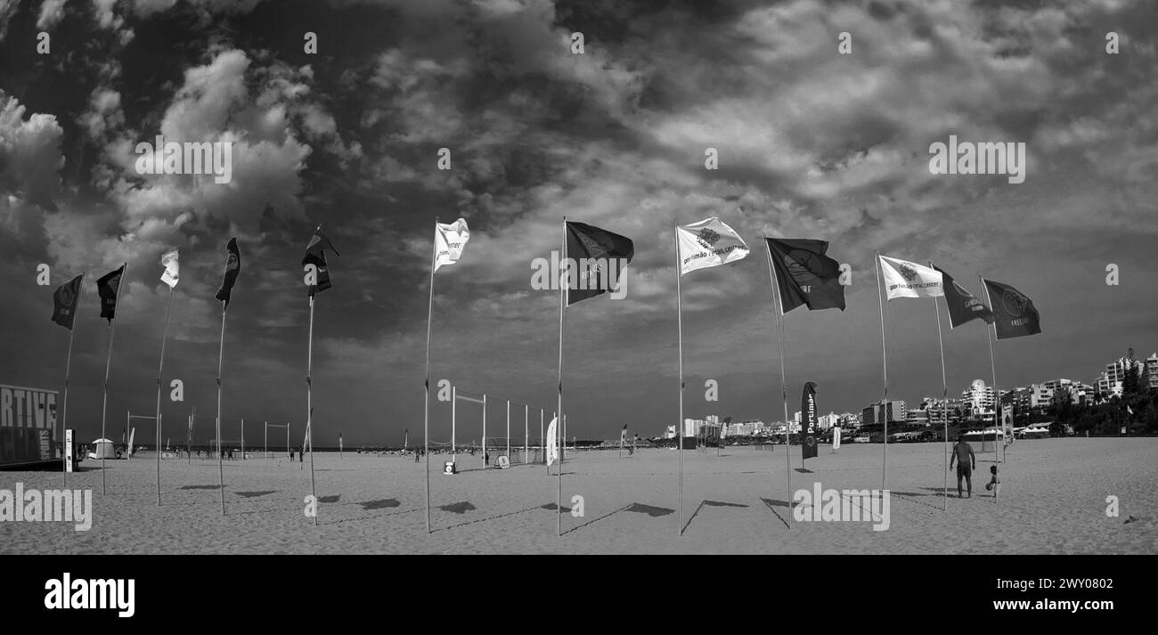 Tourists walking on the sand of Praia da Rocha next to several flags ...