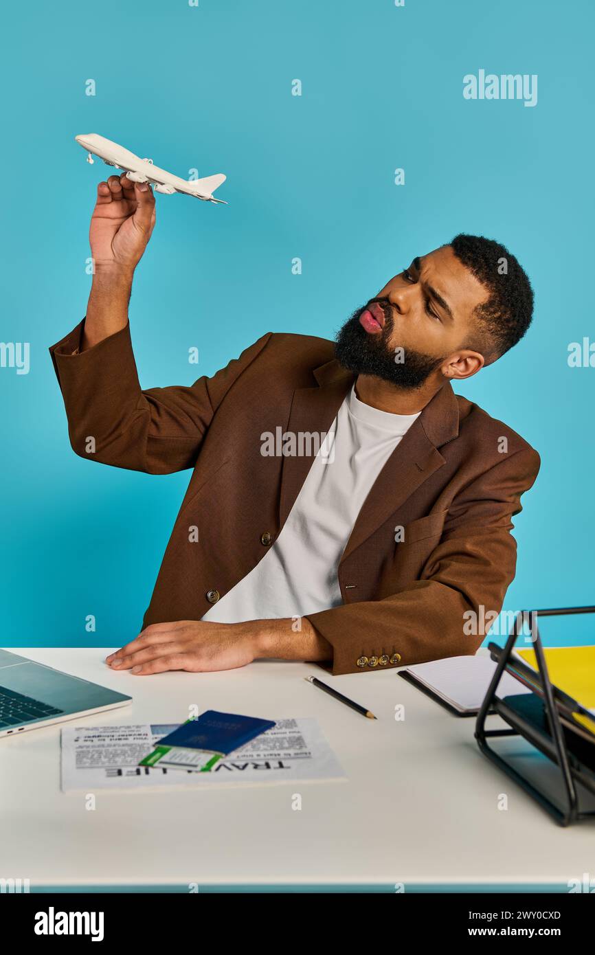 A man sits at a desk, focused on a laptop screen while a model airplane ...