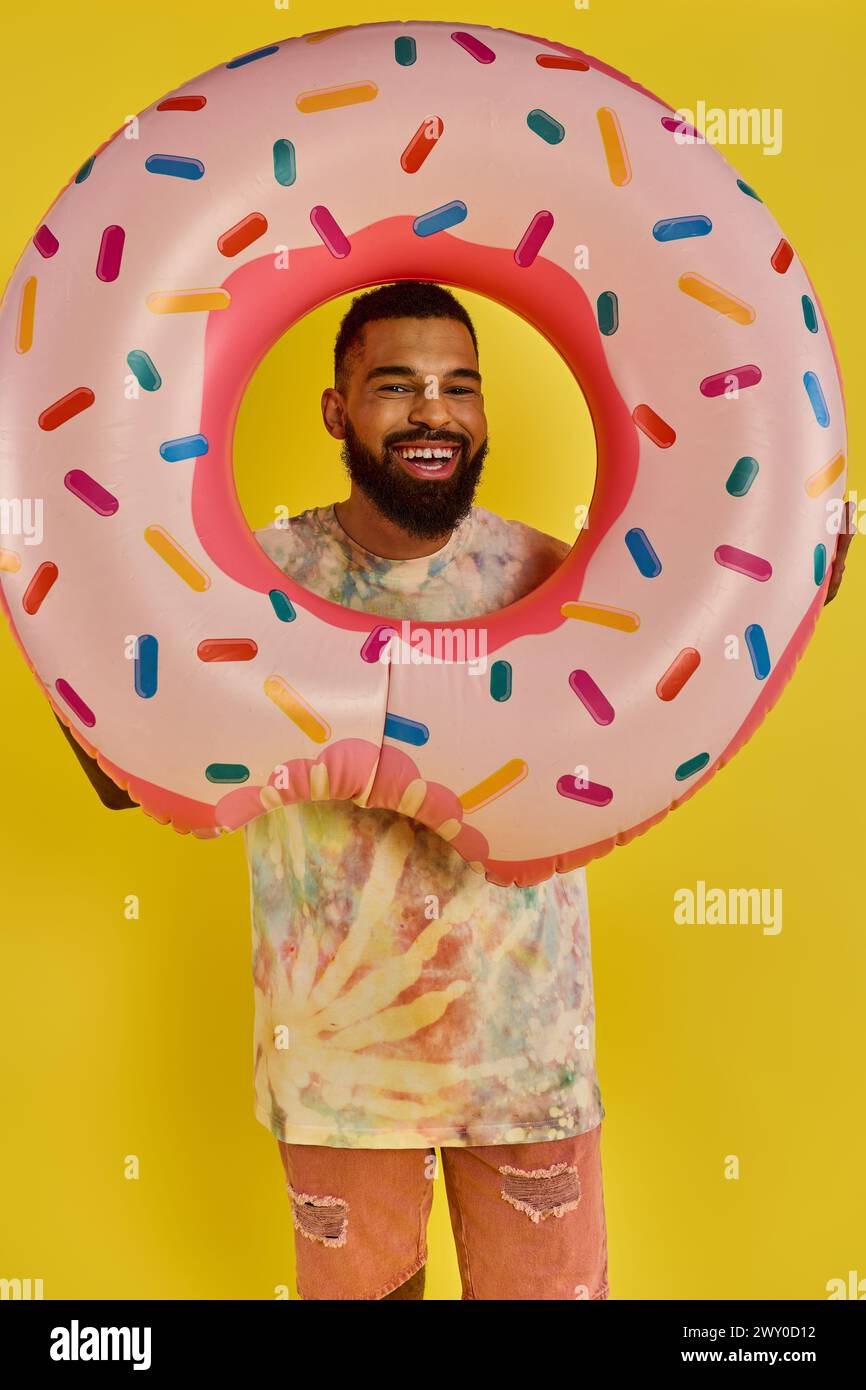 A man playfully hides his face behind a massive donut, showcasing his ...