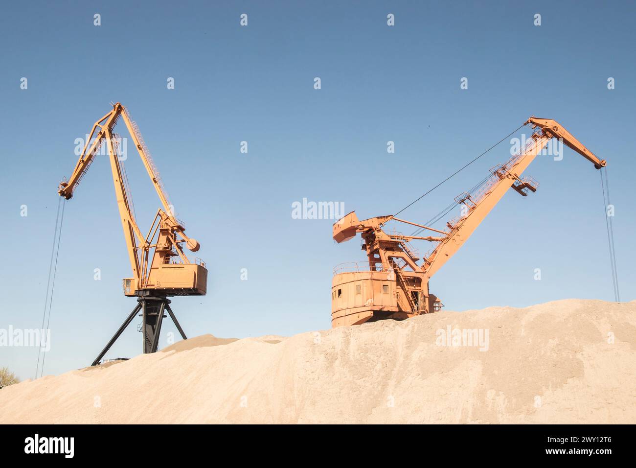 Port industrial cranes at river sand unloading depot on clear sunny day ...