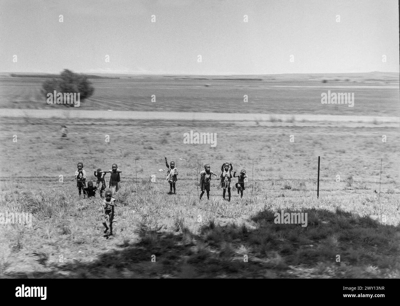 Young children by a wire fence, photographed from a moving train ...