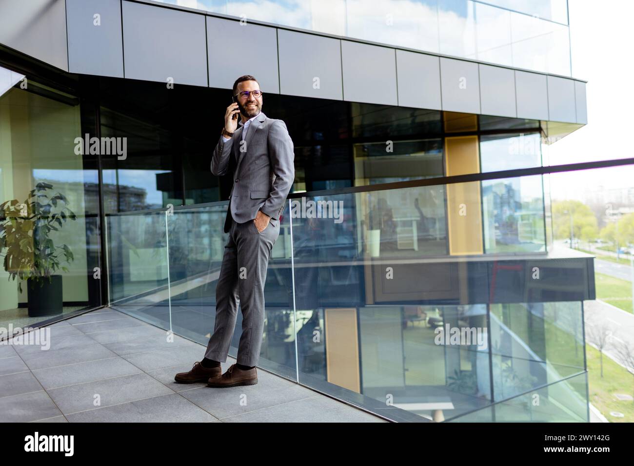 Suited man with arms crossed stands proudly before a sleek building ...