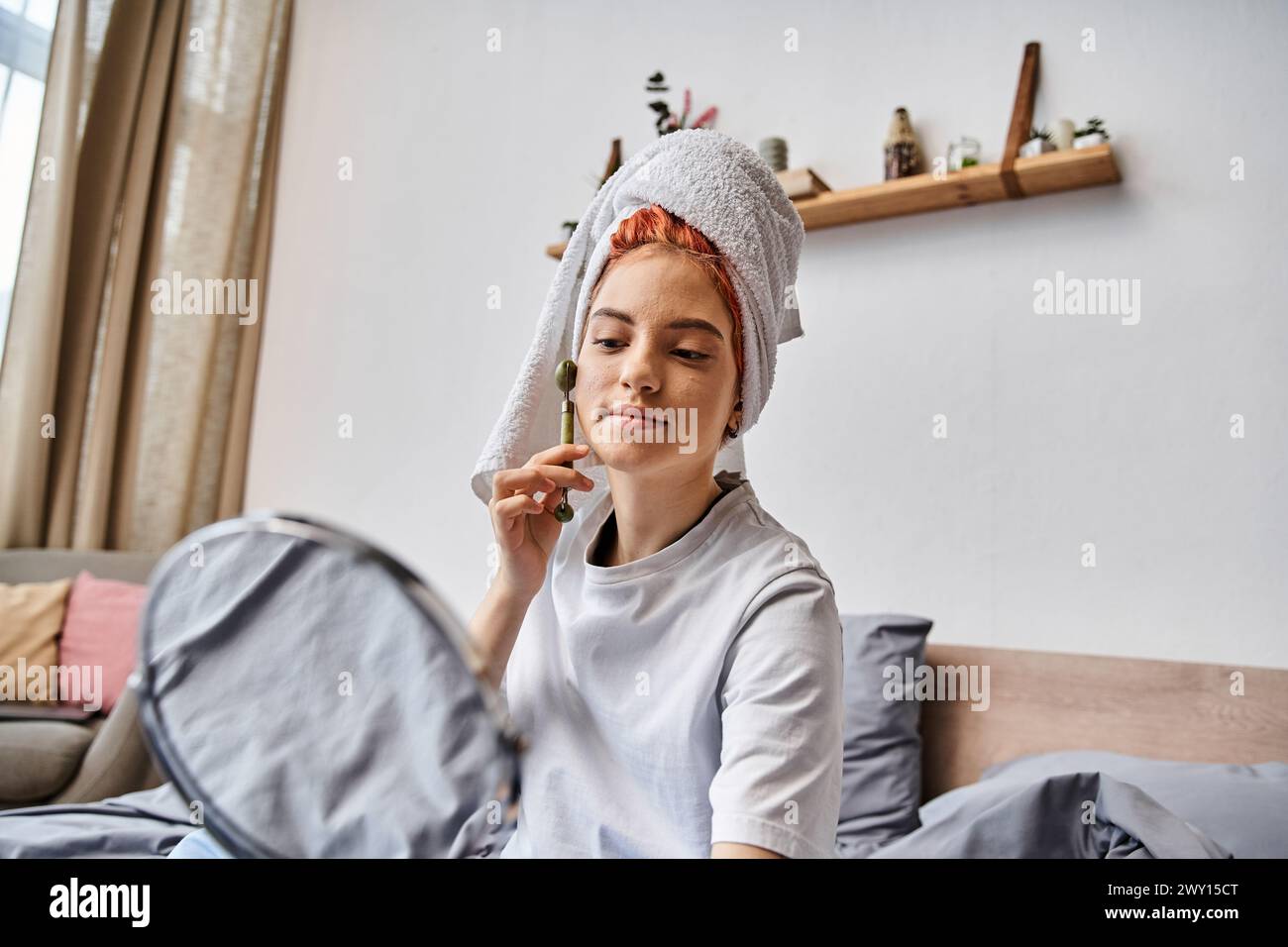 good looking queer person in cozy homewear using face roller in front ...