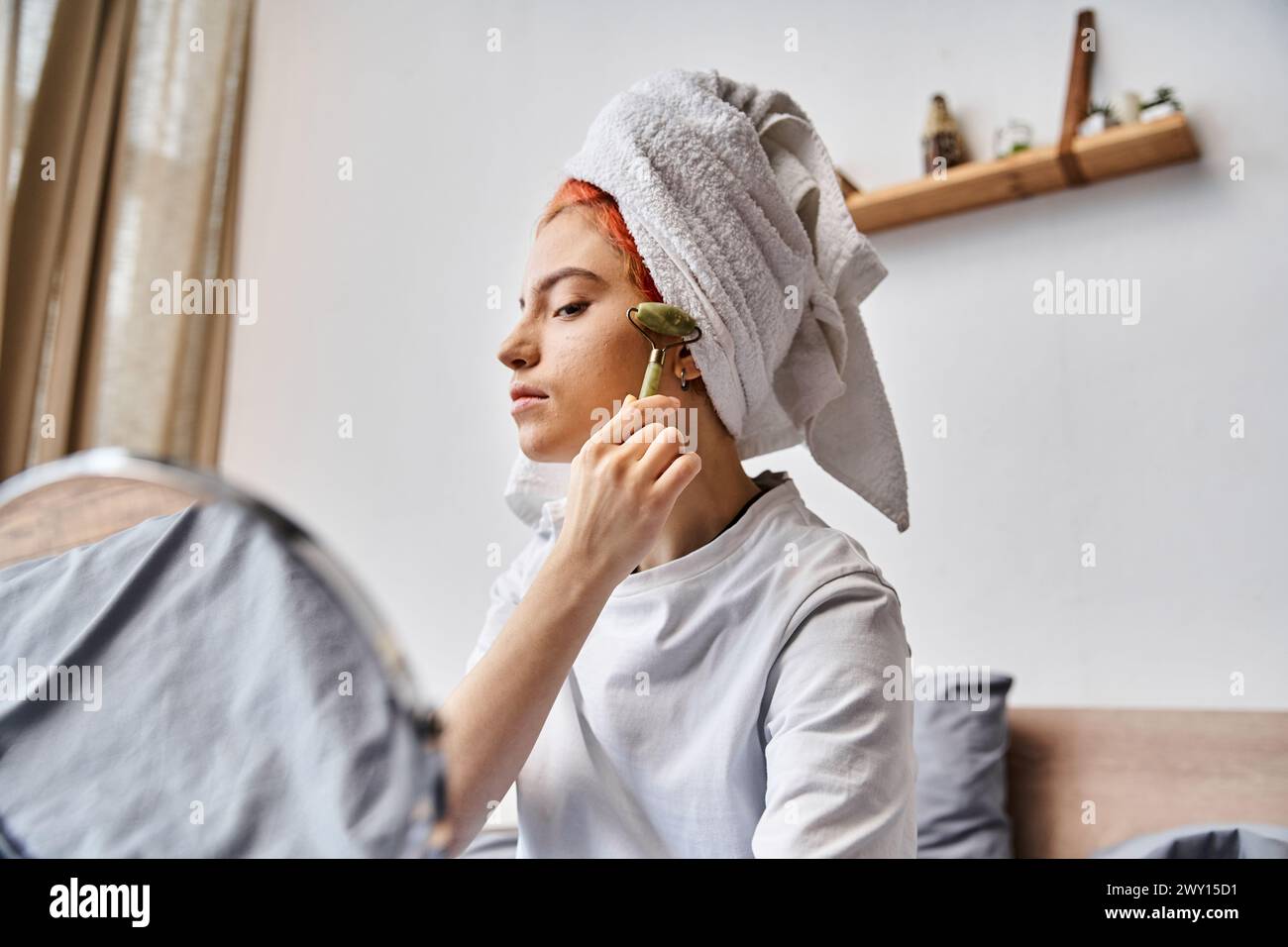 good looking queer person in cozy homewear using face roller in front ...