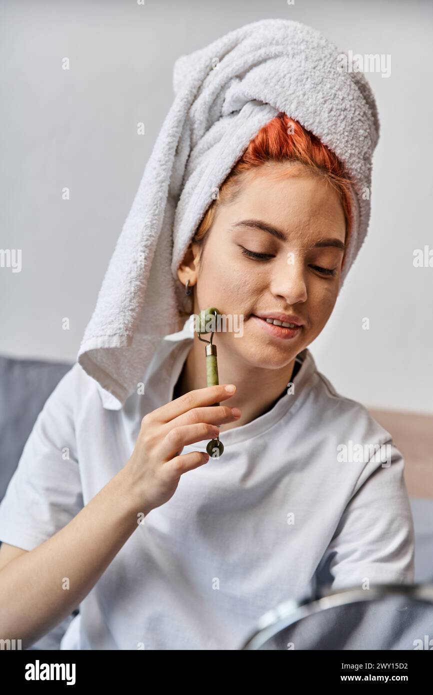attractive jolly queer person in homewear using face roller in front of ...