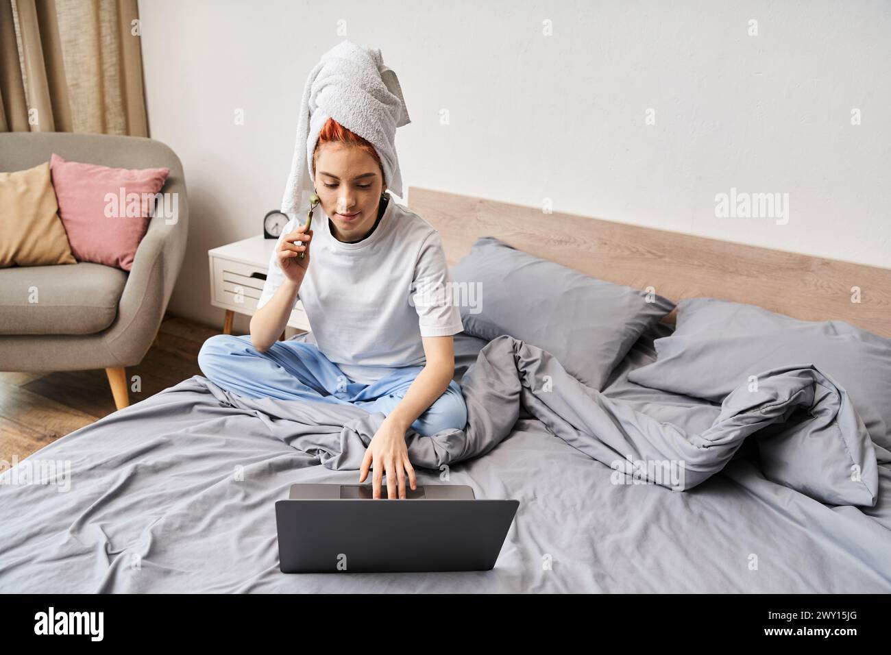 appealing red haired queer person in homewear using face roller while ...