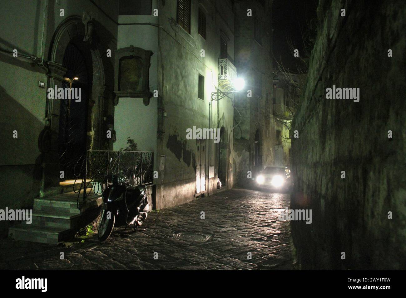 Meta, Italy. Vehicle driving at night on a cobblestone road between old ...