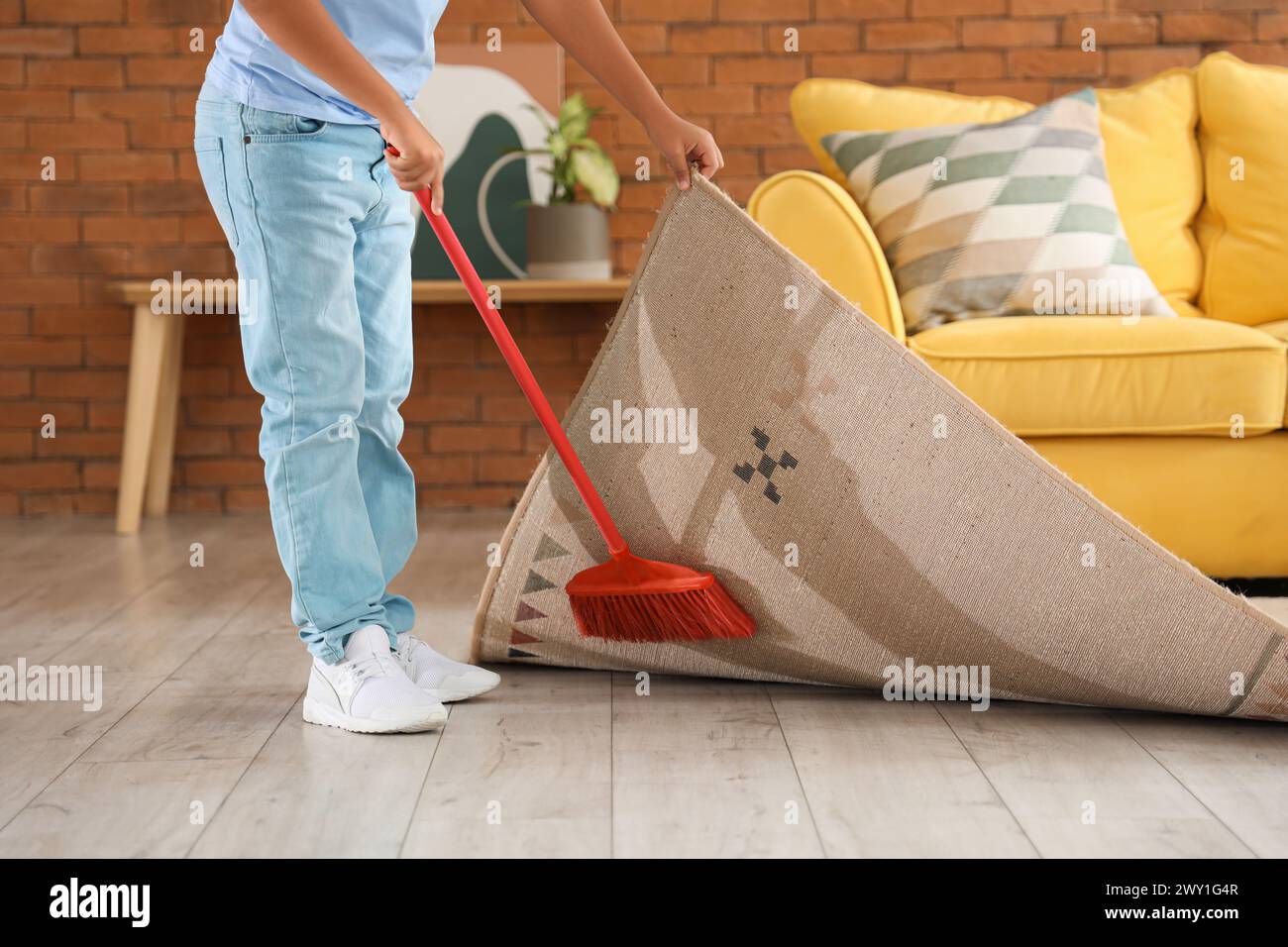 African-American boy sweeping dust under carpet with broom in living ...