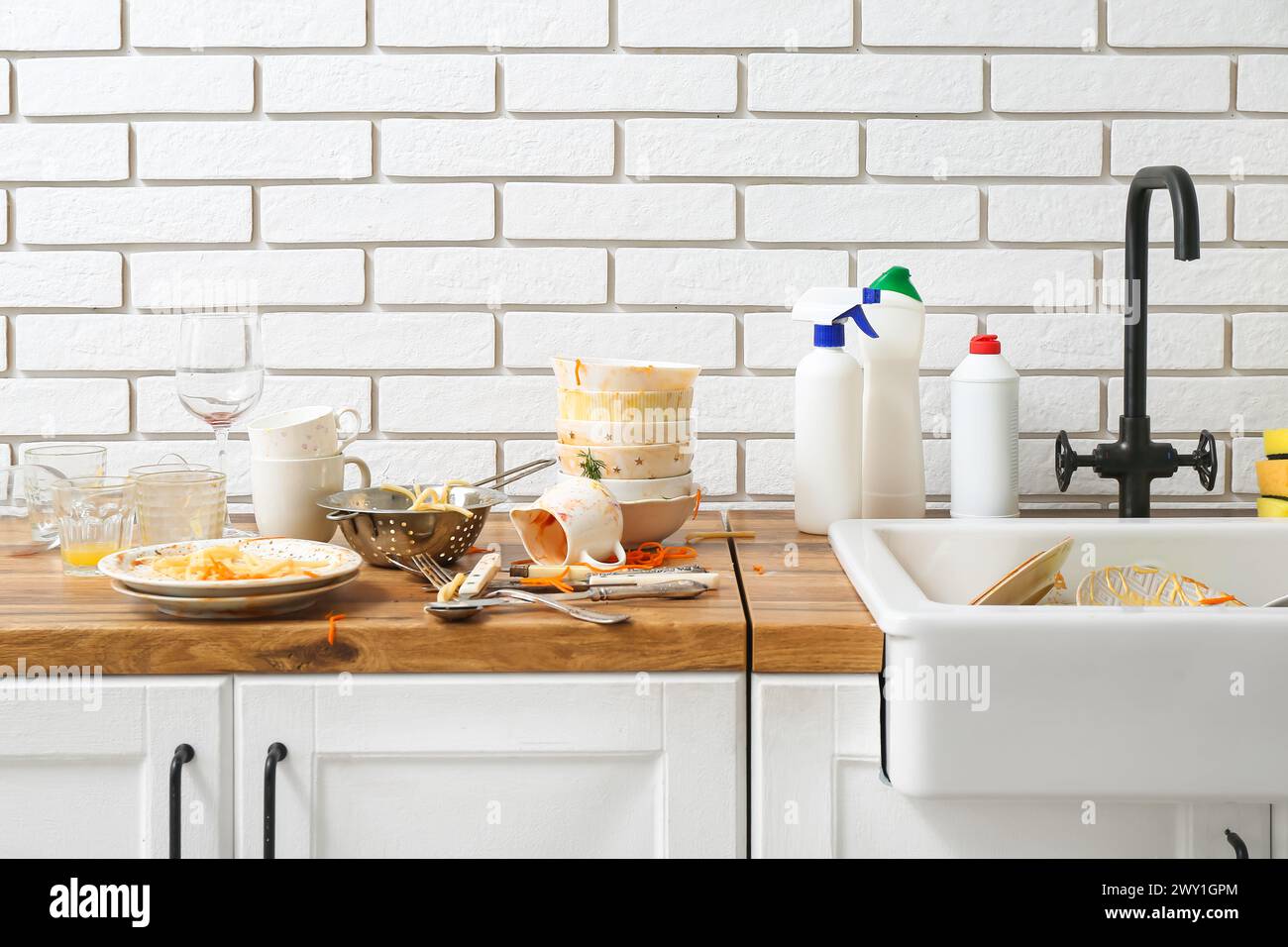 Wooden counter with ceramic sink and dirty dishes near white brick wall ...