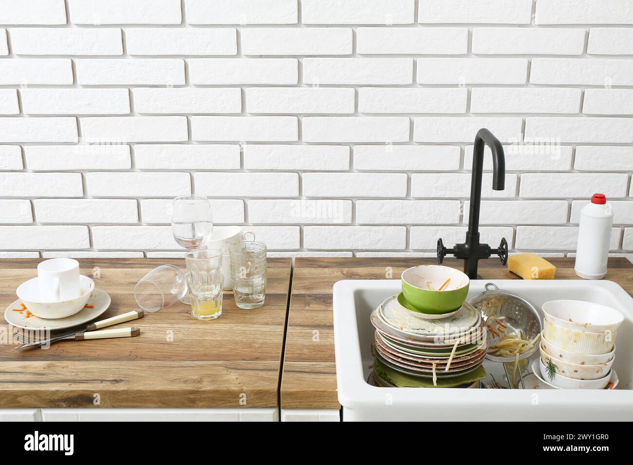 Wooden counter with ceramic sink and dirty dishes near white brick wall ...