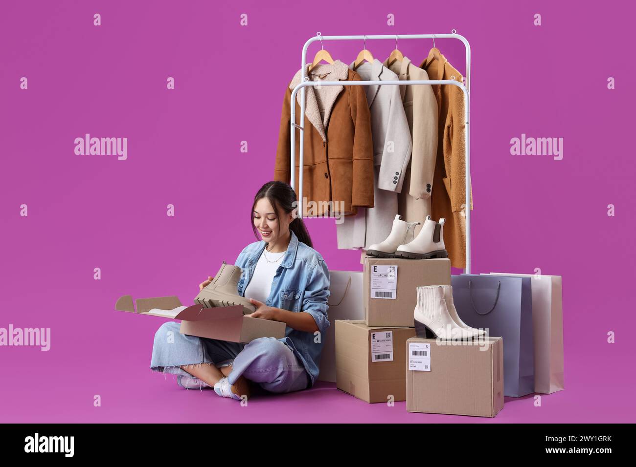 Young Asian seller with shoes, shopping bags and clothes rack on purple ...
