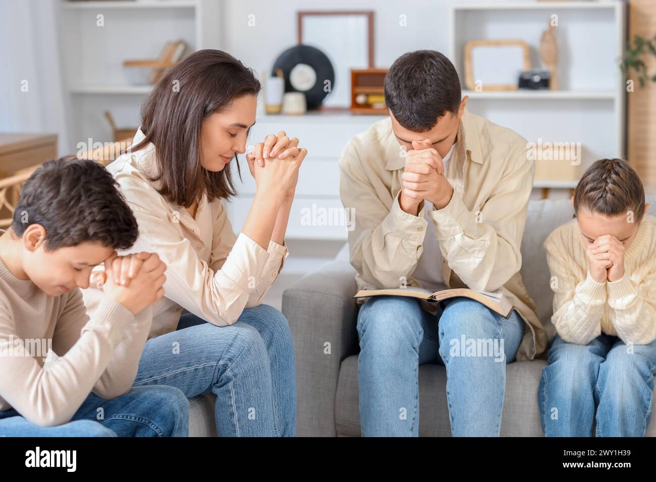 Family with Holy Bible praying on sofa at home Stock Photo - Alamy