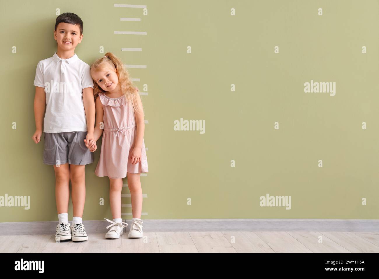Cute little kids measuring height near green wall Stock Photo - Alamy