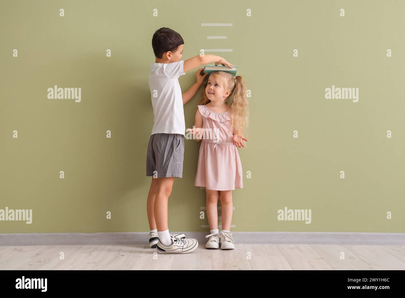 Cute little kids measuring height near green wall Stock Photo - Alamy