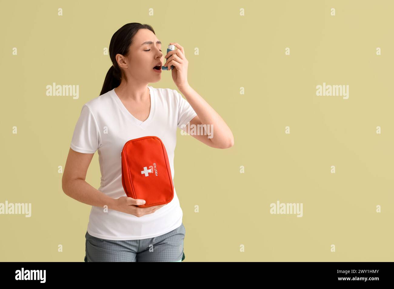 Sporty young woman with first aid kit using inhaler on green background ...