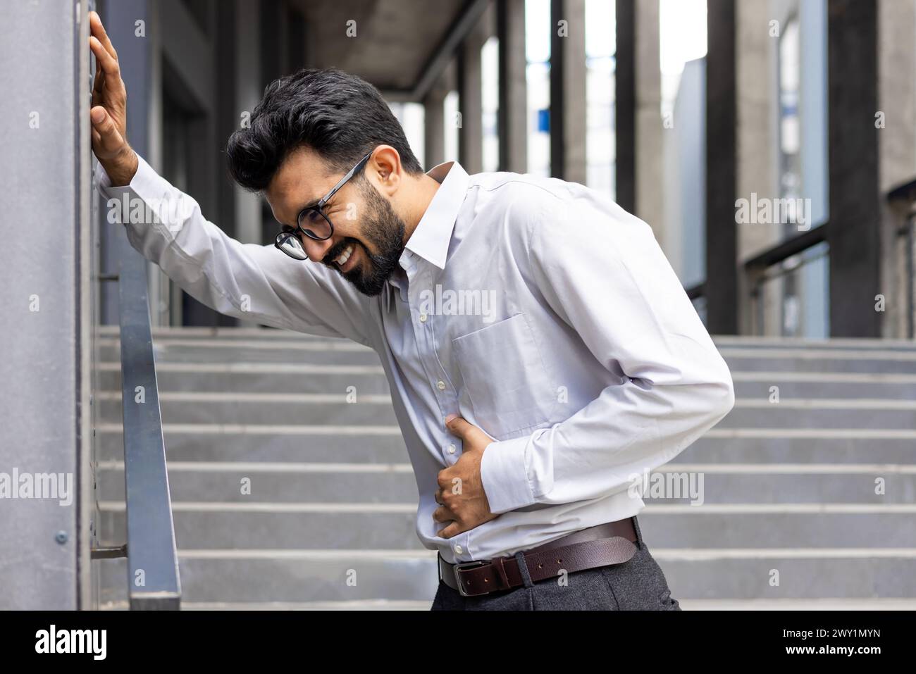 Young Indian man suffering from stomach pain, holding hands to abdomen ...