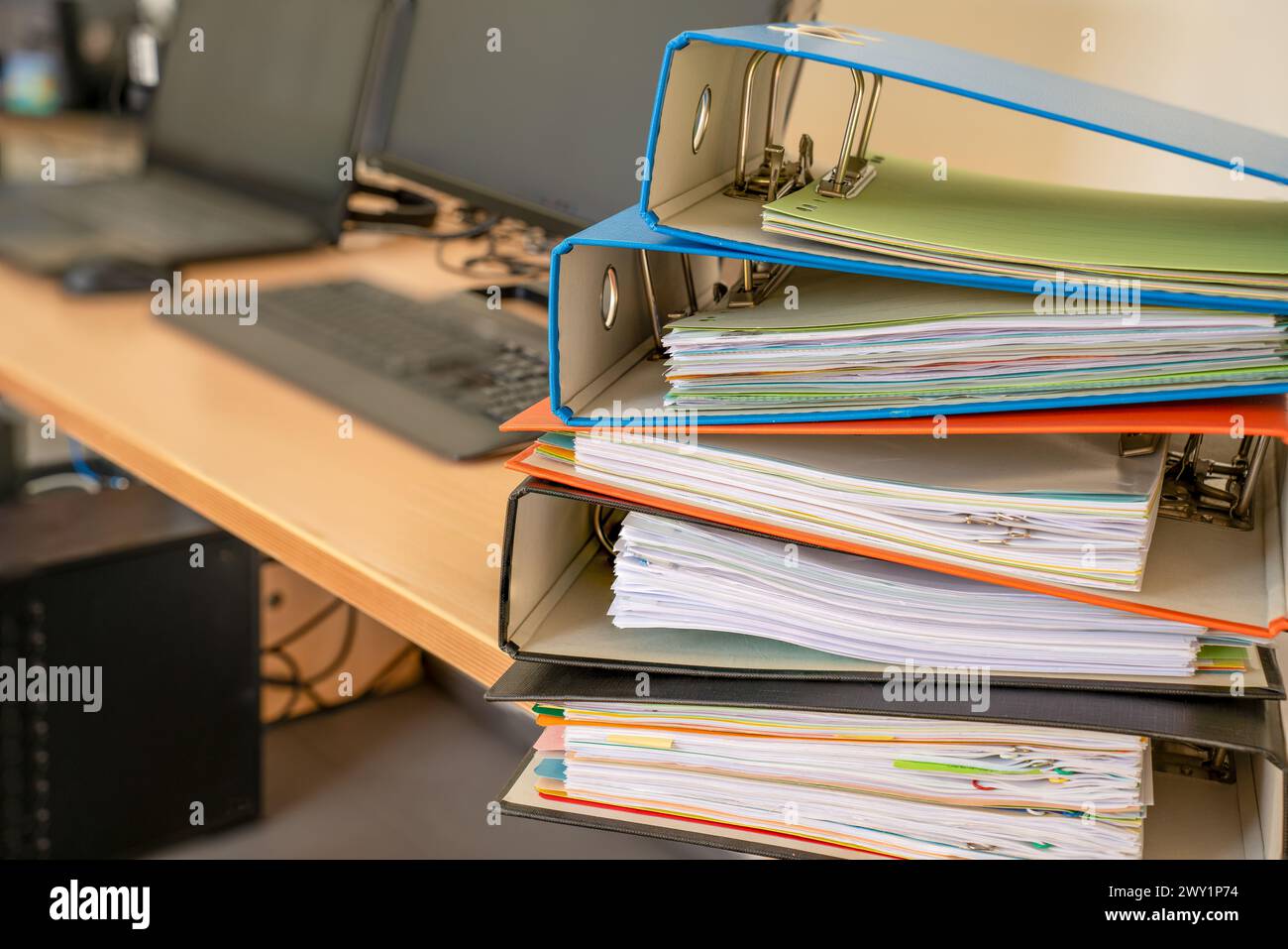 Pile of file folders stacked on desk, in front of computer and laptop ...