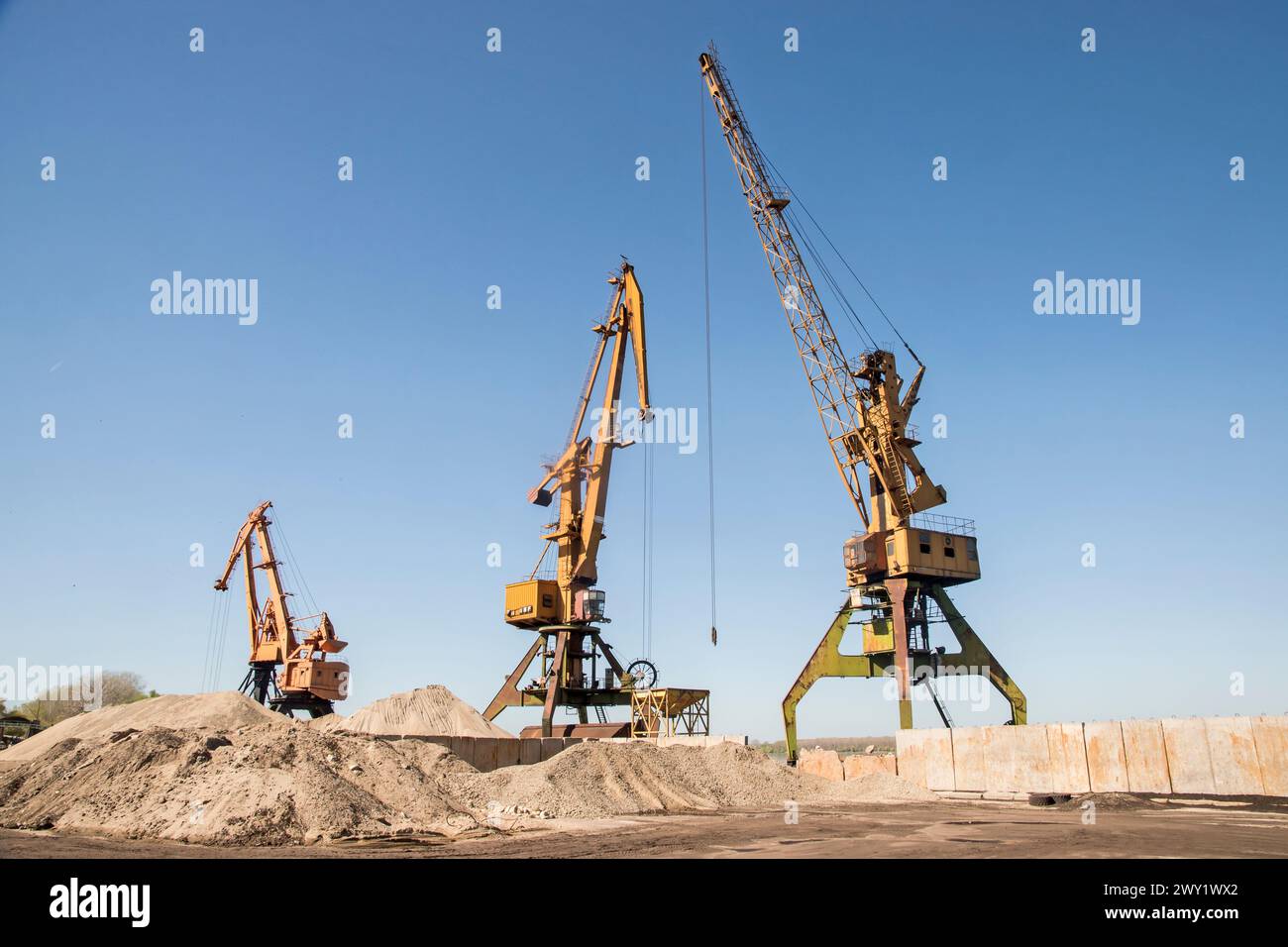 Port industrial cranes at river sand unloading depot on clear sunny day ...