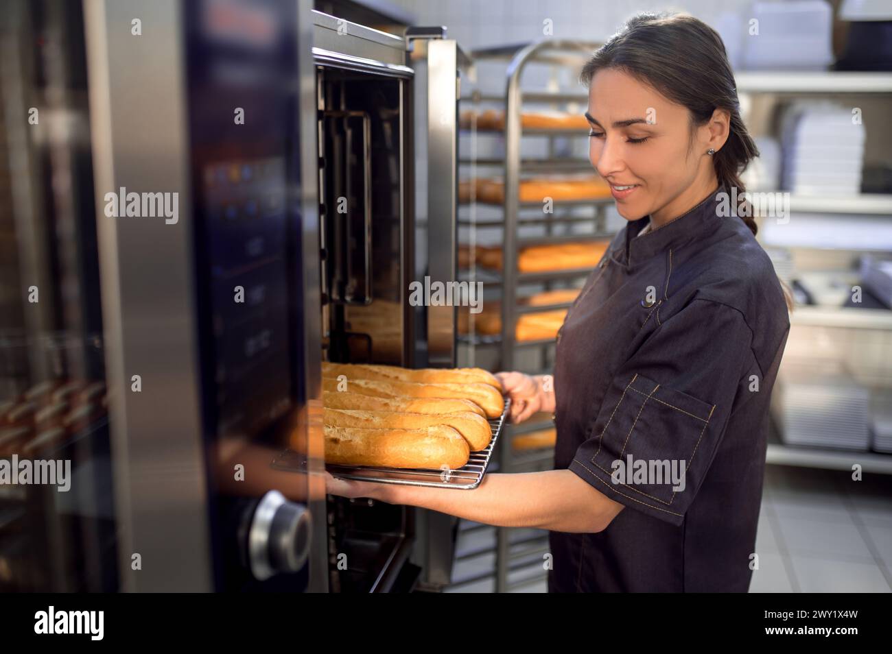 Woman baker using electrical oven for baking French baguettes Stock ...