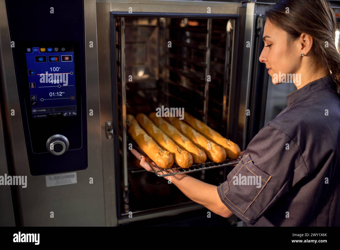 Woman baker using electrical oven for baking French baguettes Stock ...